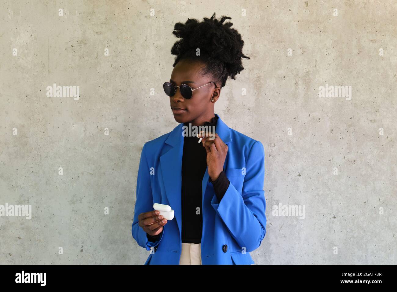 African woman putting on wireless earbuds, with blue jacket suit and ...