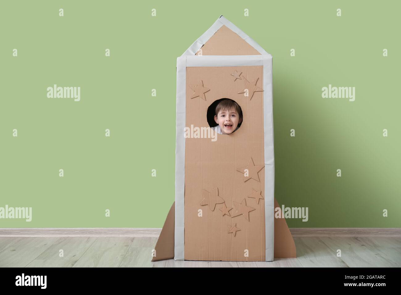 Cute little boy in cardboard rocket on color background Stock Photo - Alamy