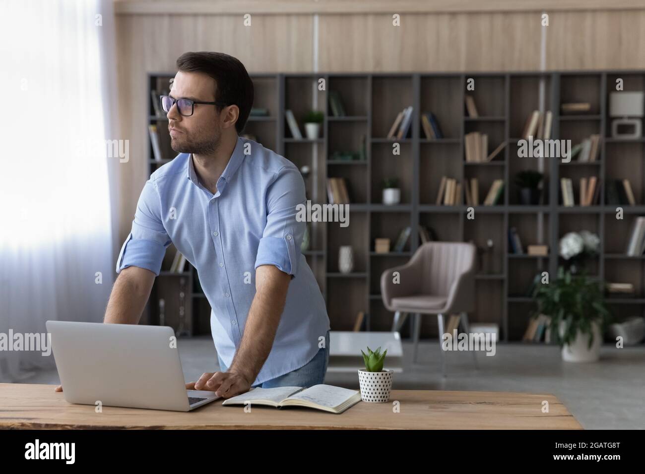 Male student stand by desk with laptop look away think Stock Photo - Alamy
