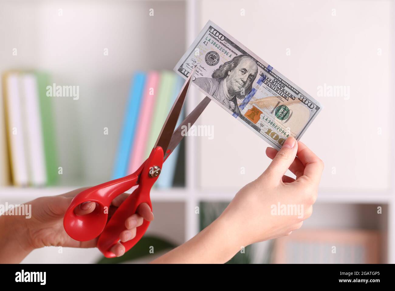Hands with scissors cutting dollar banknote, on blurred interior ...