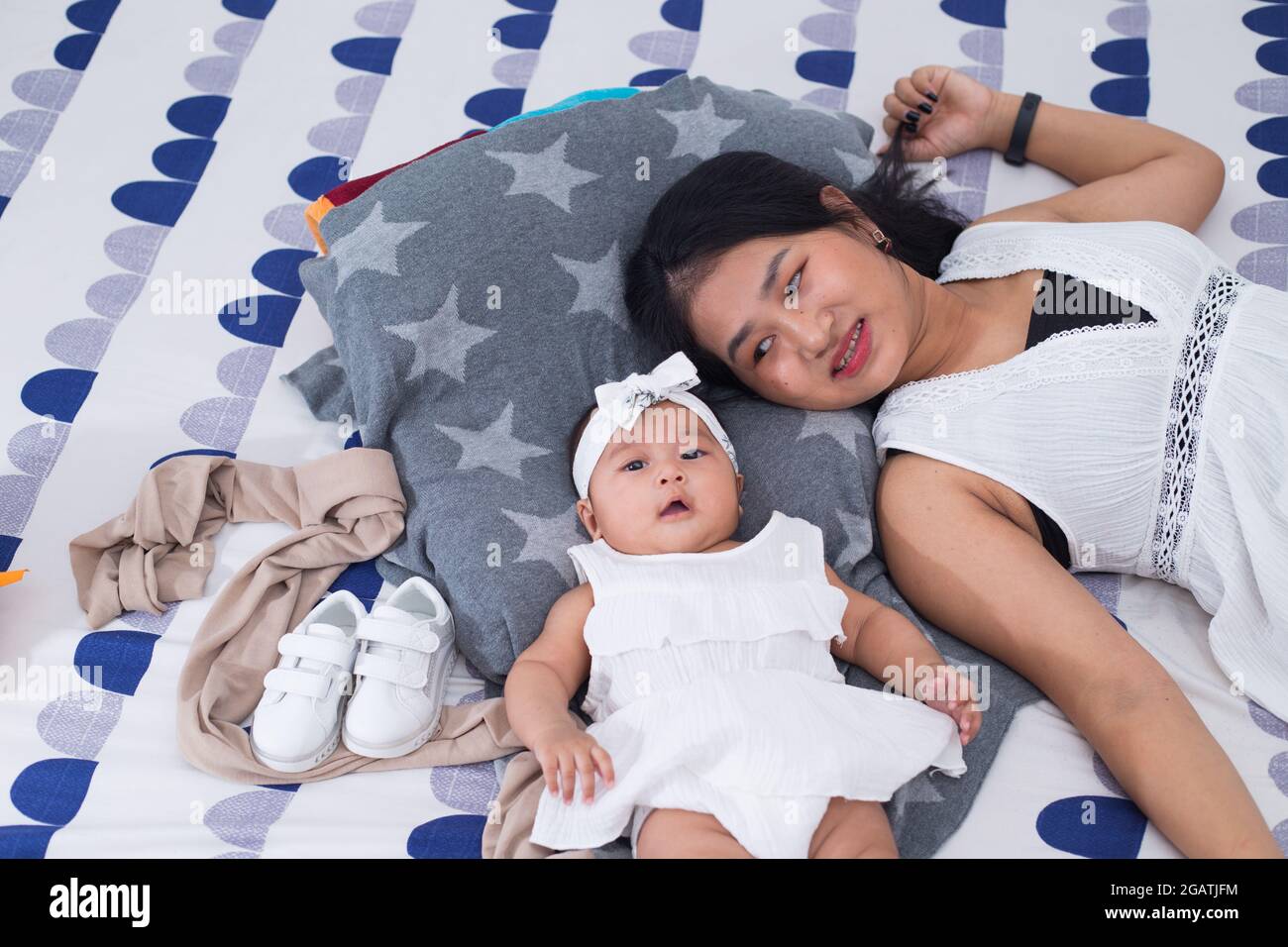 A southeast asian baby girl in a white dress and headband lying on the ...