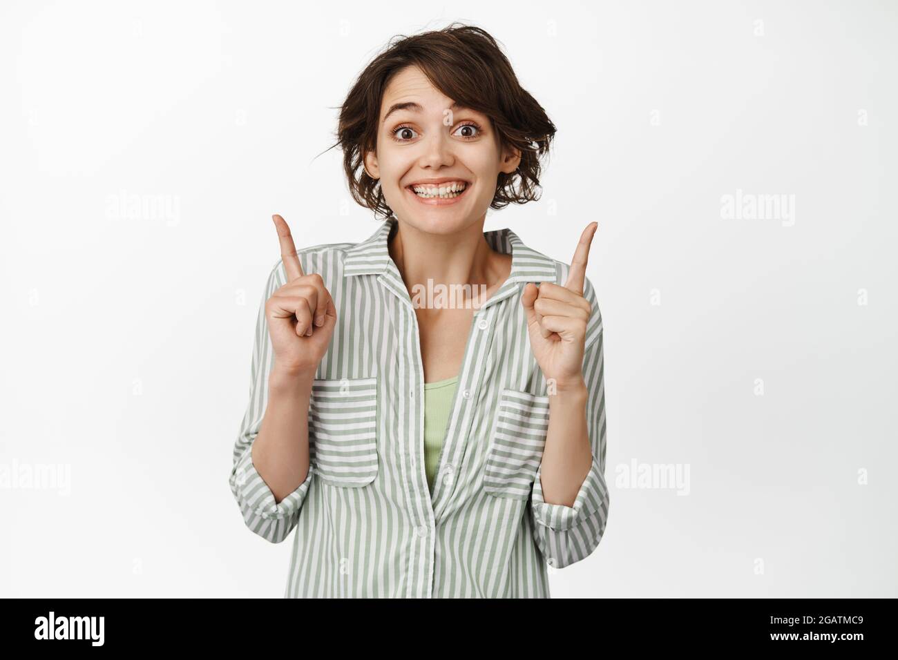 Portrait of excited brunette girl smiling, pointing fingers sideways ...