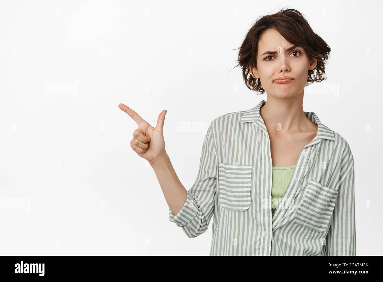 Disappointed frowning girl, pointing finger left, showing smth ...