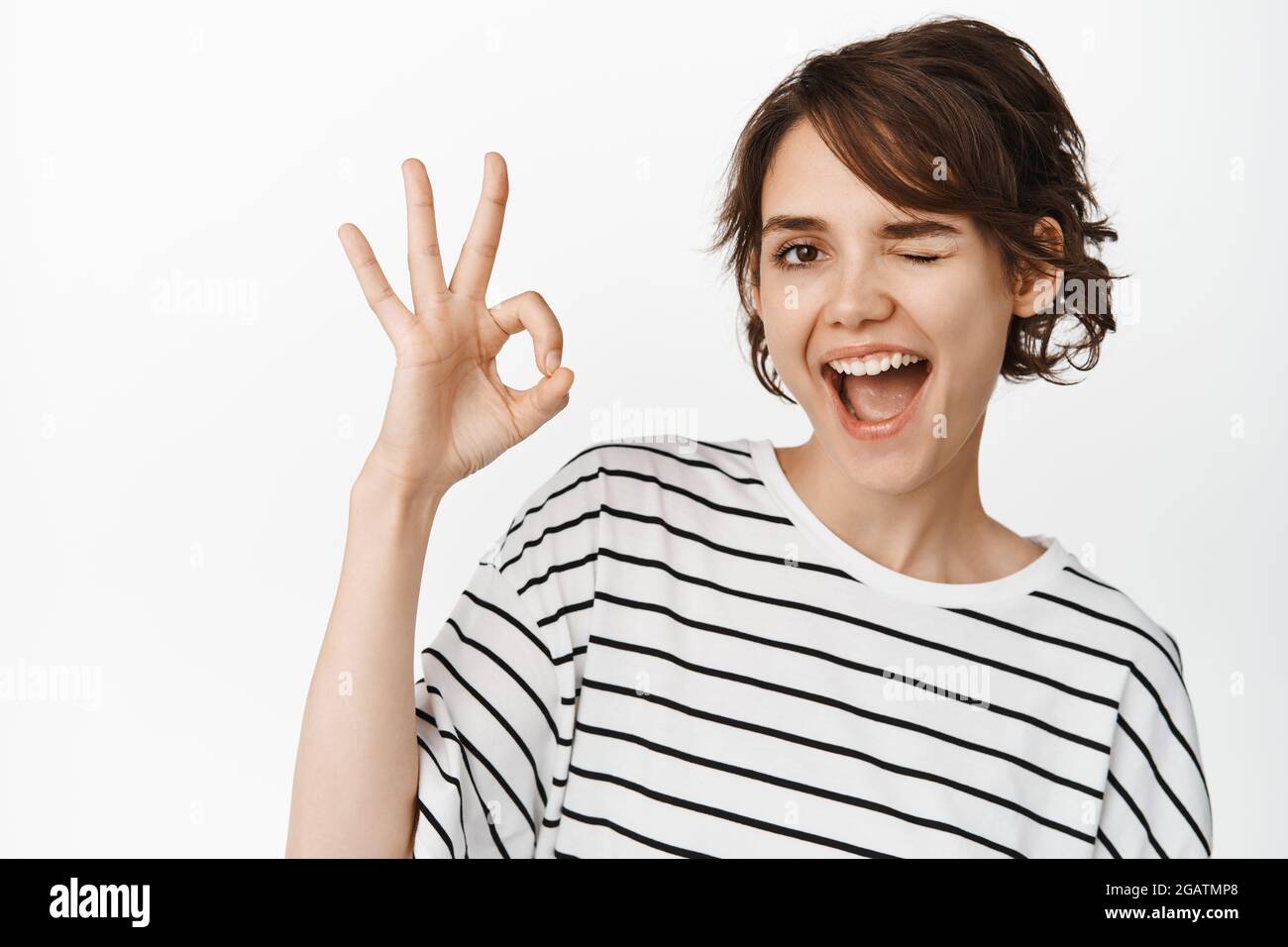 Cheeky brunette girl, coquettish woman winking and smiling satisfied ...