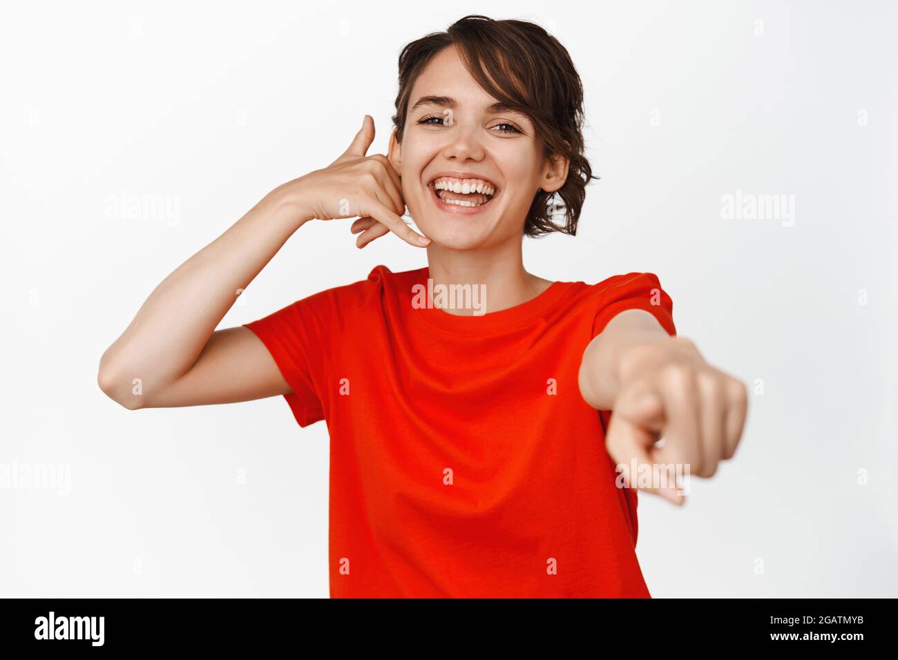 Call us. Smiling pretty girl pointing finger at camera, laughing and ...