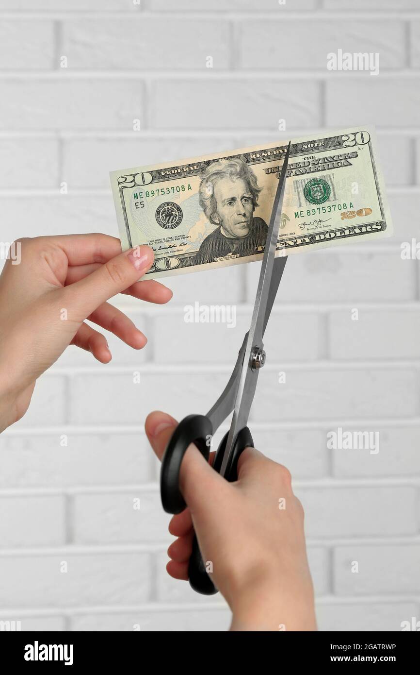 Hands with scissors cutting money on white brick wall background Stock ...
