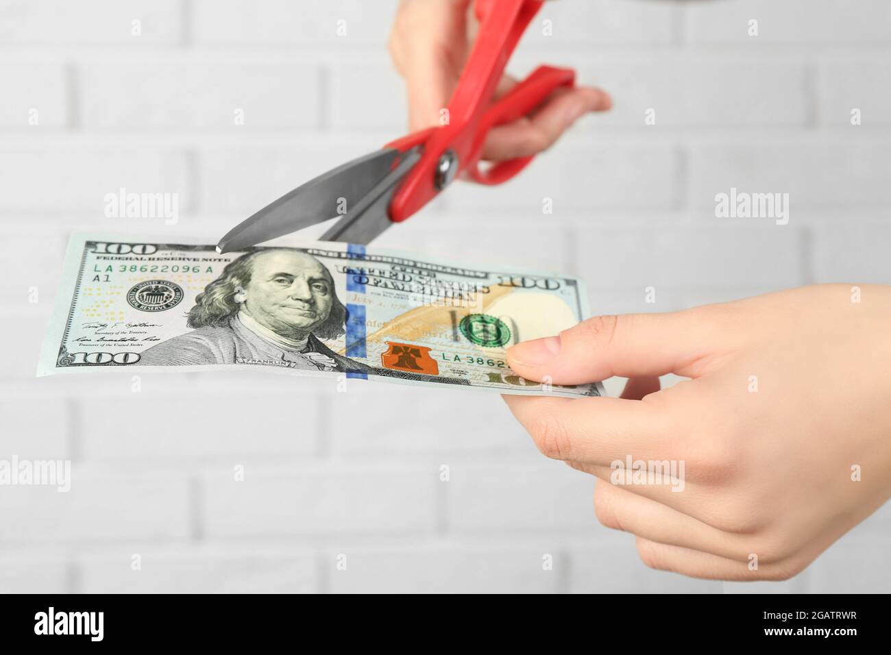 Hands with scissors cutting money on white brick wall background Stock ...
