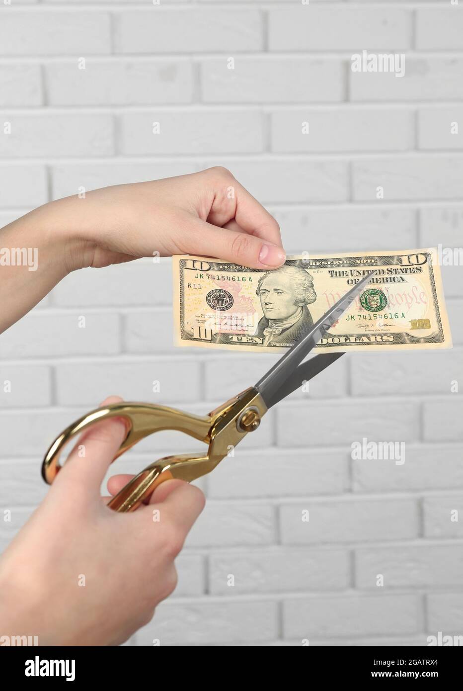 Hands with scissors cutting money on white brick wall background Stock ...