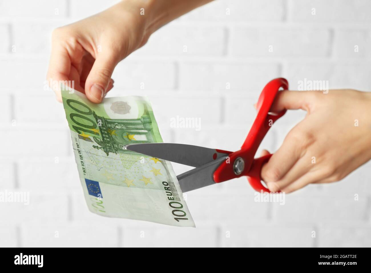 Hands with scissors cutting money on white brick wall background Stock ...