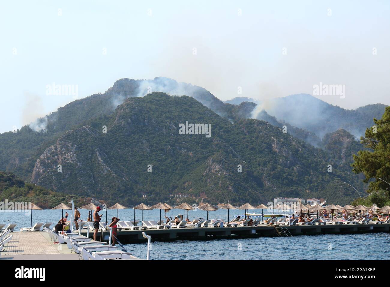 People sunbathe on a pier as smoke rises from a forest fire in Marmaris ...
