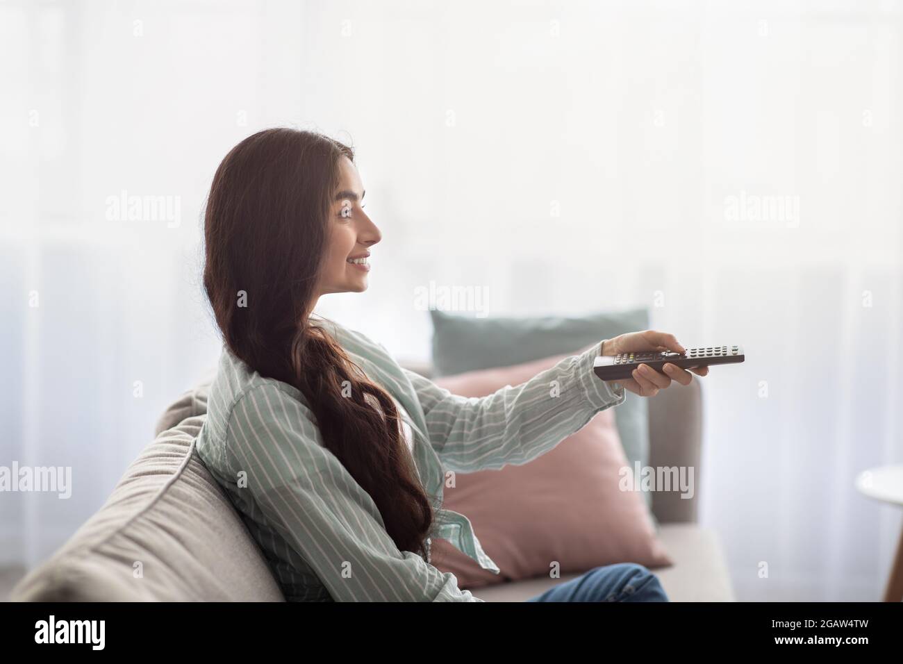 Side view of lovely Indian lady with remote control watching TV on ...