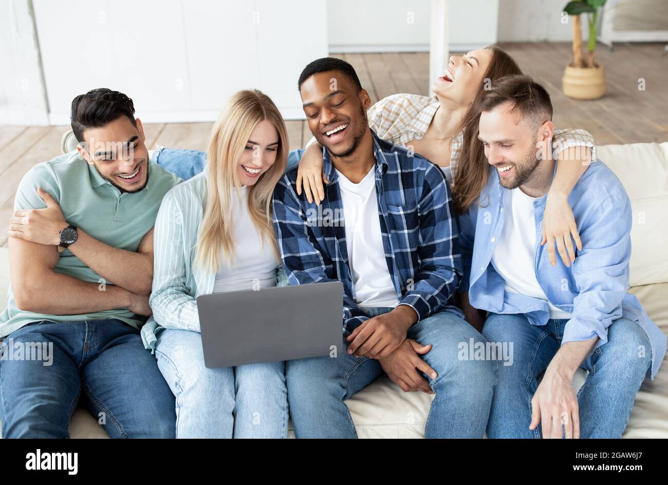 Happy multiethnic friends using laptop computer, sitting on couch in ...