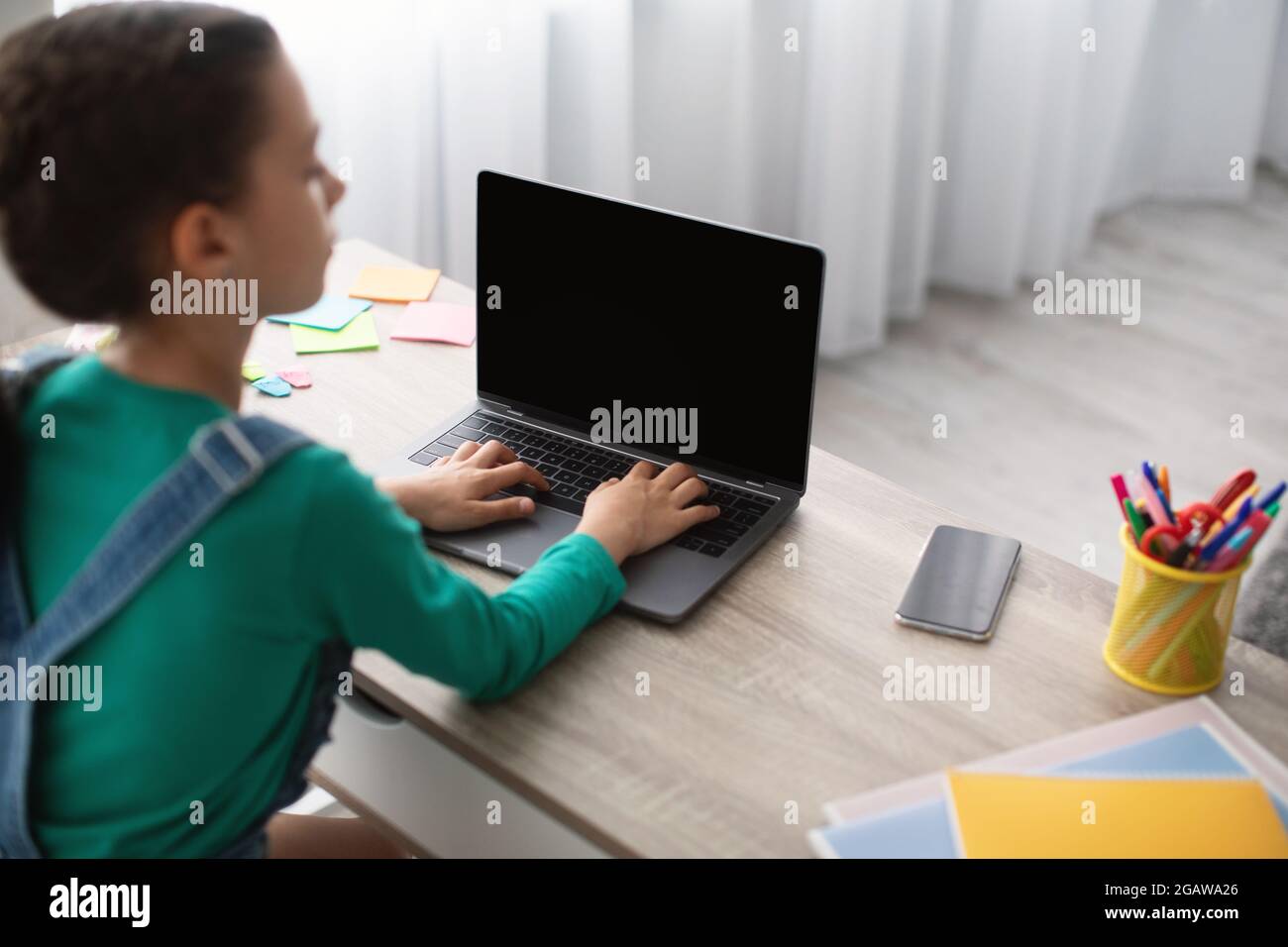 Over the shoulder view portrait of little student girl sitting at desk ...