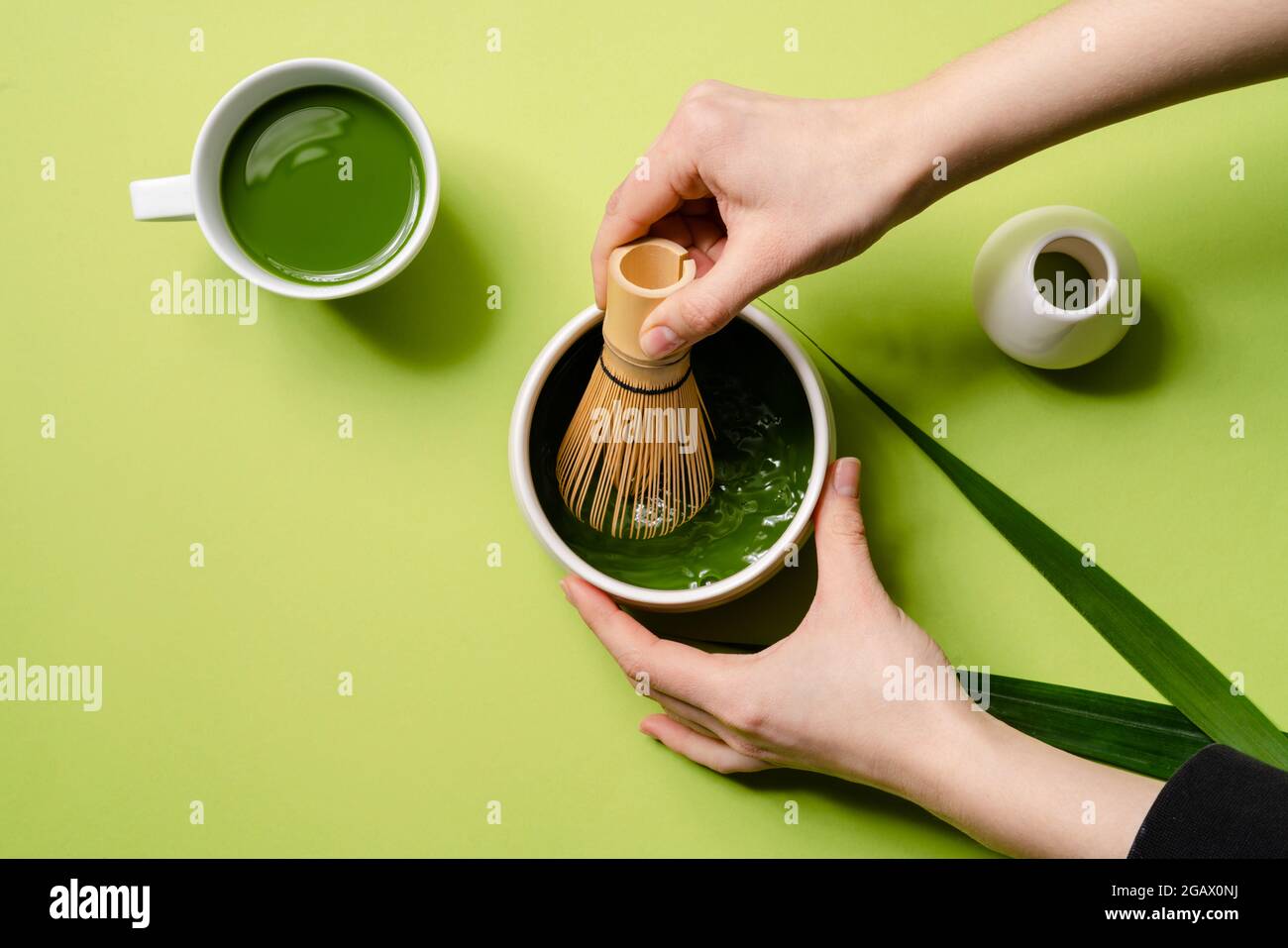 A close-up shot of a woman's hands mixing a matcha in a cup in a green ...