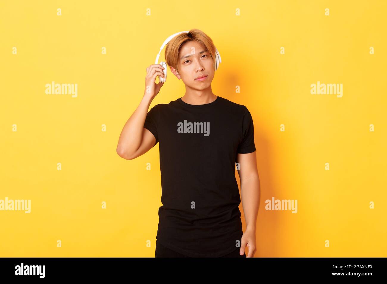 Young handsome asian guy with blond hair, take-off headphones to listen ...