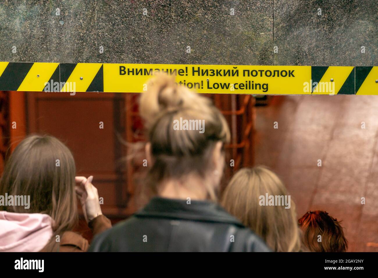 Back view of young women going under low ceiling with the warning sign ...