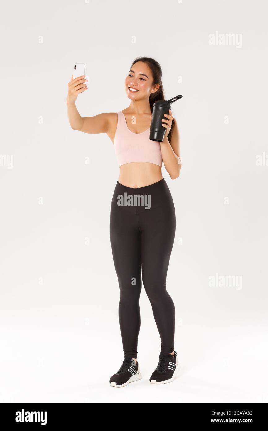 Full length of smiling slim and healthy asian girl taking selfie ...