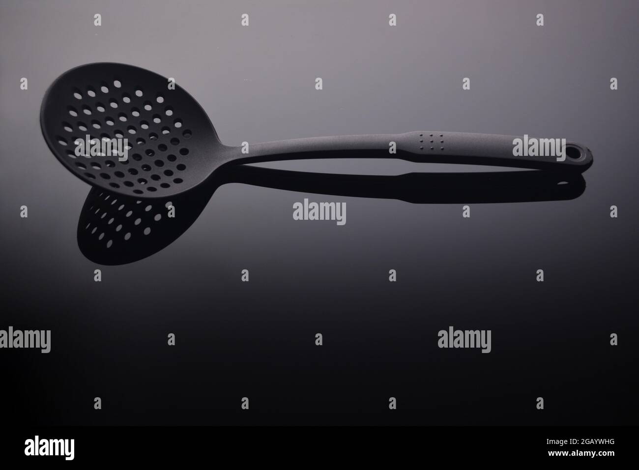 Black plastic kitchen skimmer, on a black background with a gradient ...