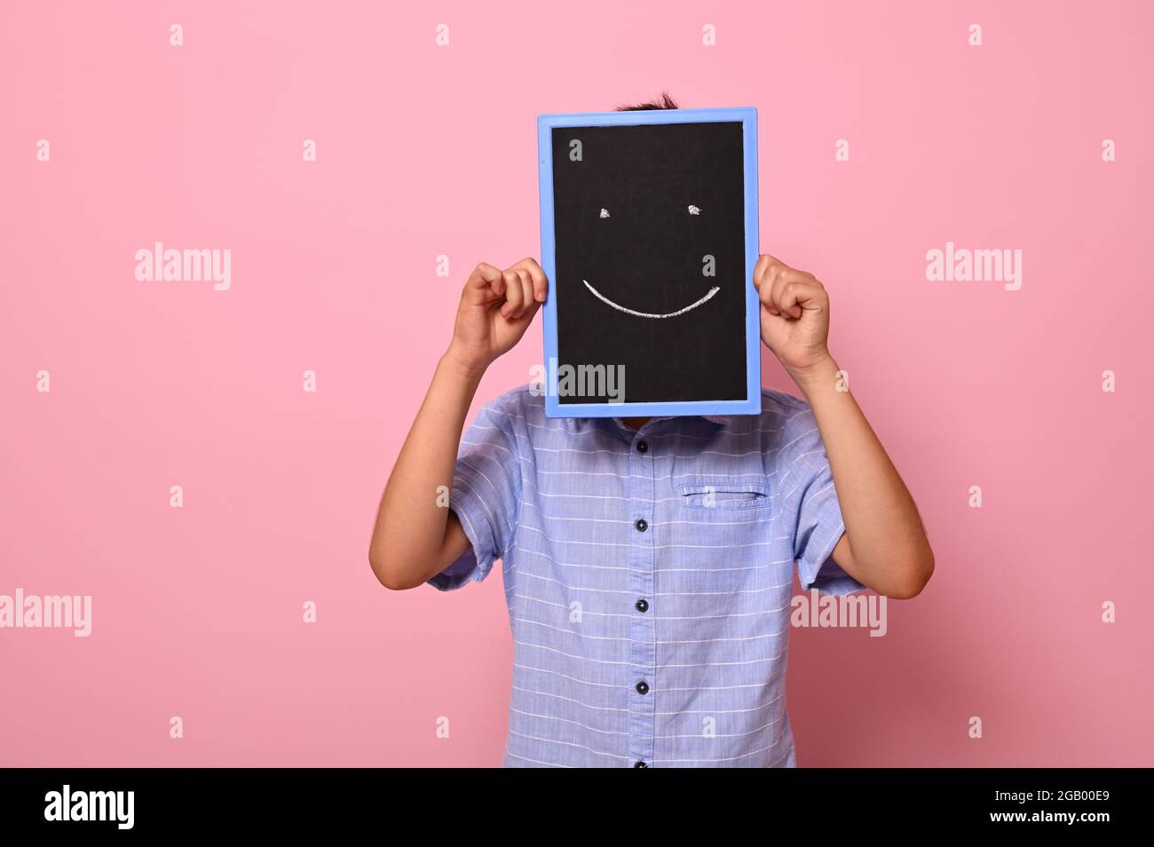 Unrecognizable school boy covers his face with a chalkboard with drawn ...