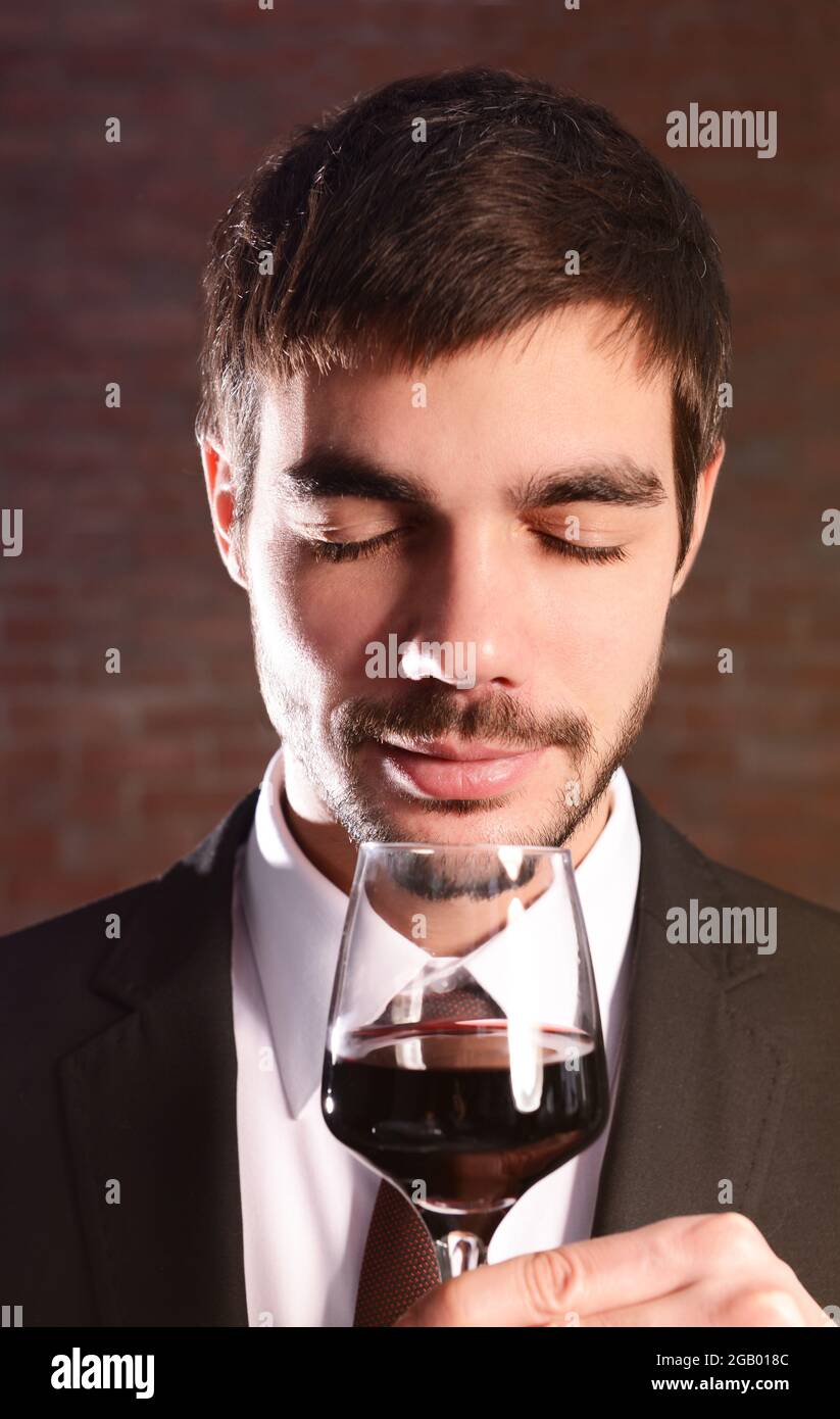 Man sniffing red wine in glass on brick wall background Stock Photo - Alamy