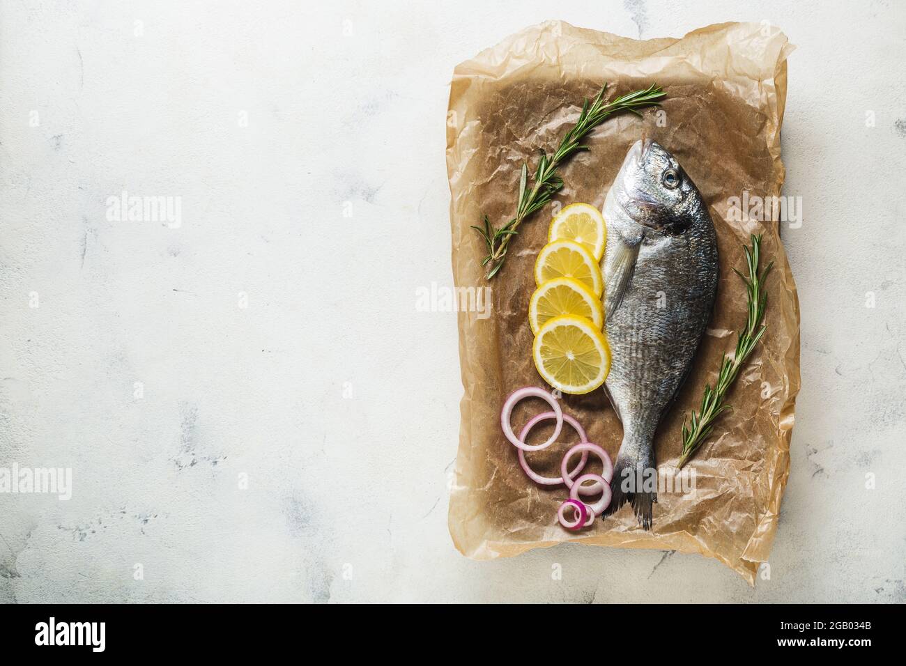 Raw Dorado fish prepared for cooking with slices of lemon, rosemary and ...