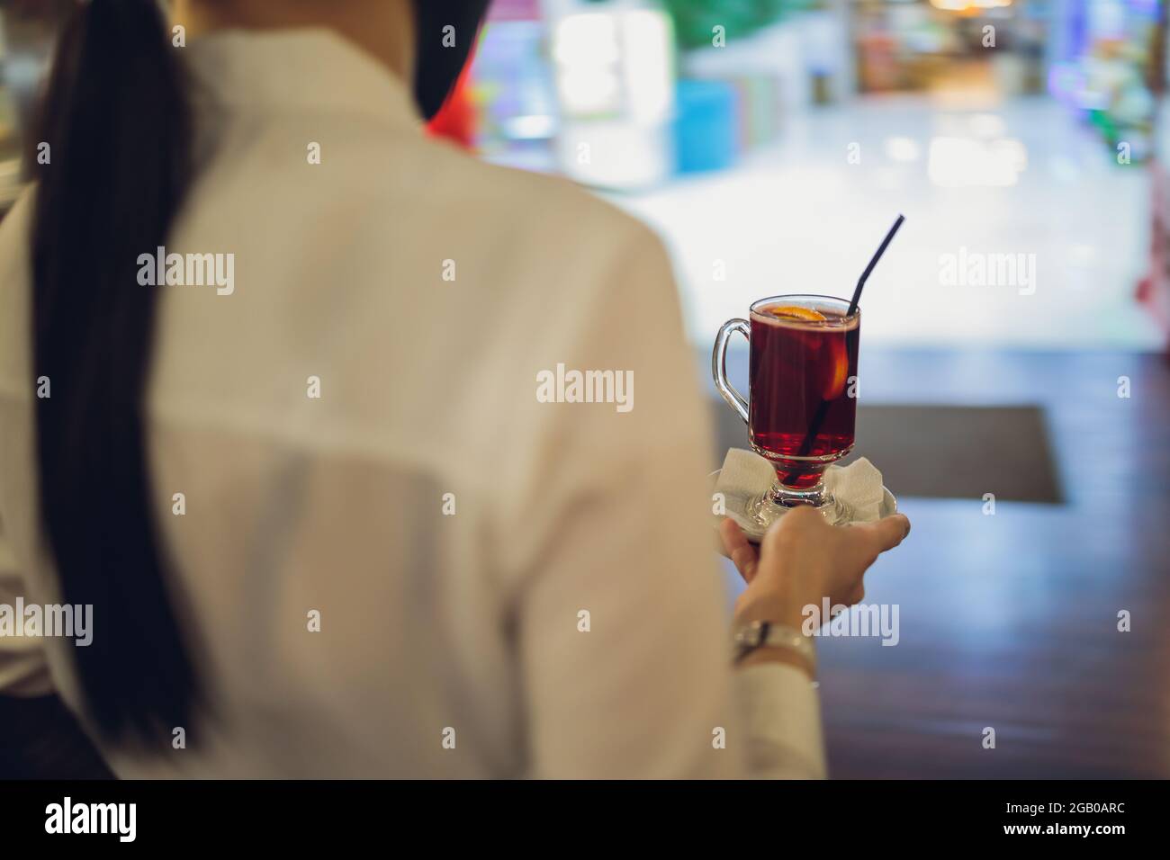 Hand of young waitress with cup of tea or coffee carrying it to one of ...