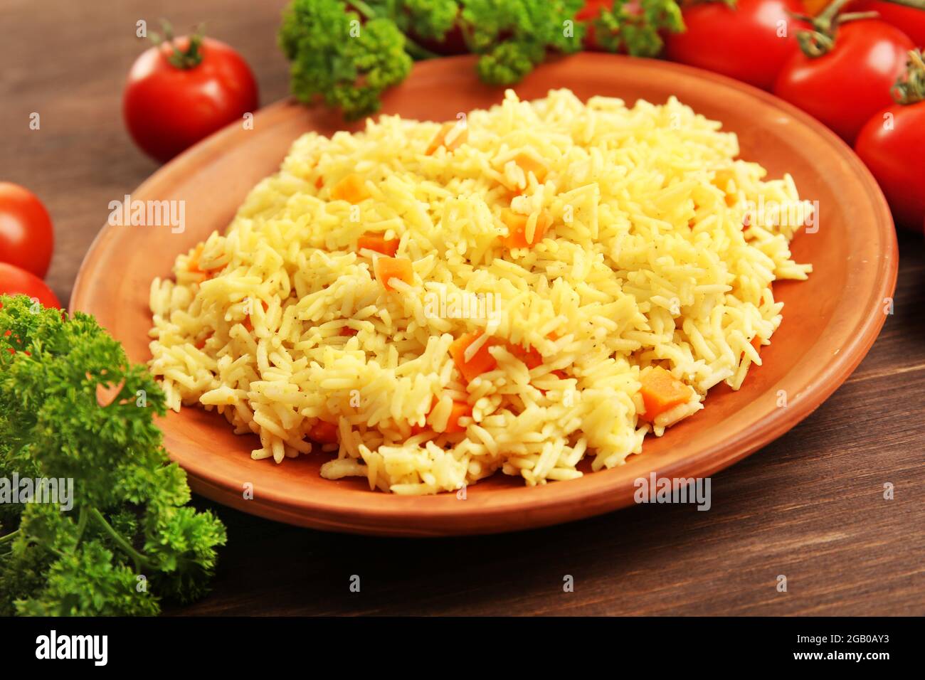 Stewed rice with a carrot on a brown plate over wooden background ...