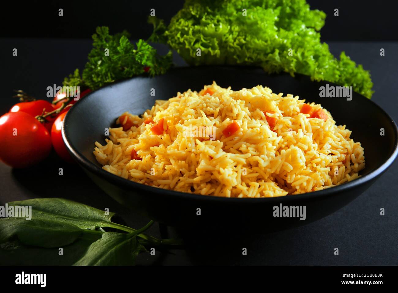 Stewed rice with a carrot on a plate over black background, close up ...