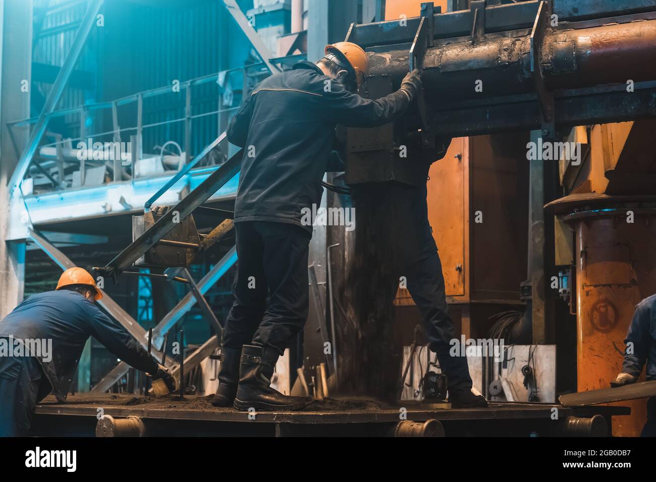 Workers in process of work with large mold iron cast on steel mill ...
