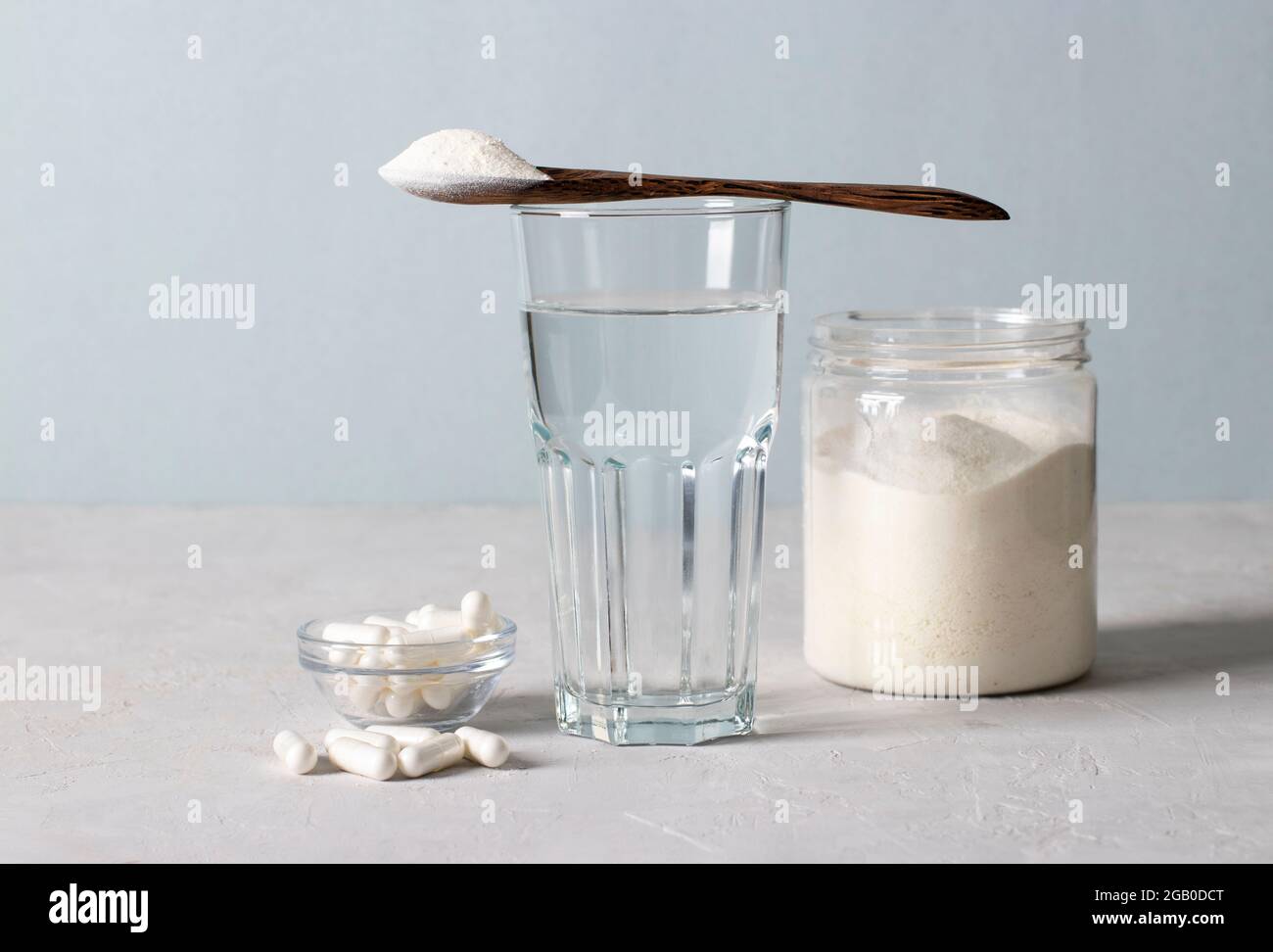 Collagen powder in spoon on glass of water, collagen capsules and jar ...