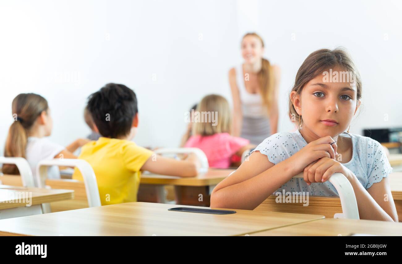Positive tween schoolgirl sitting at school desk at lesson in class ...