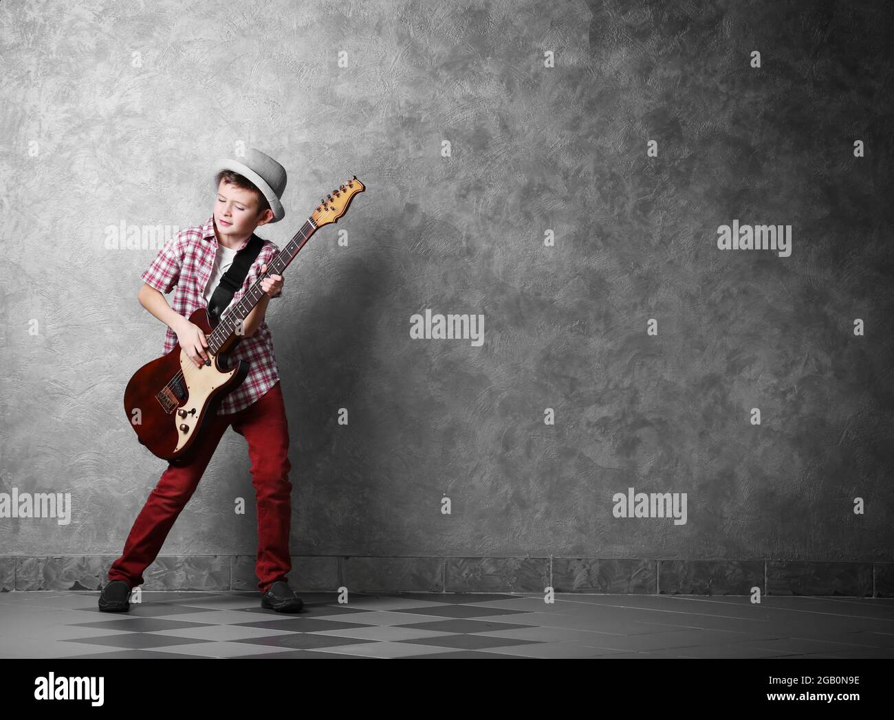 Little boy playing guitar on a grey wall background Stock Photo - Alamy