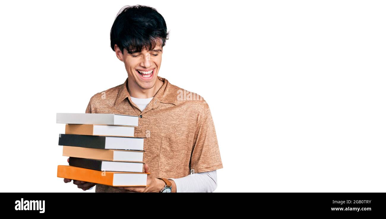 Handsome hipster young man holding a pile of books smiling and laughing ...