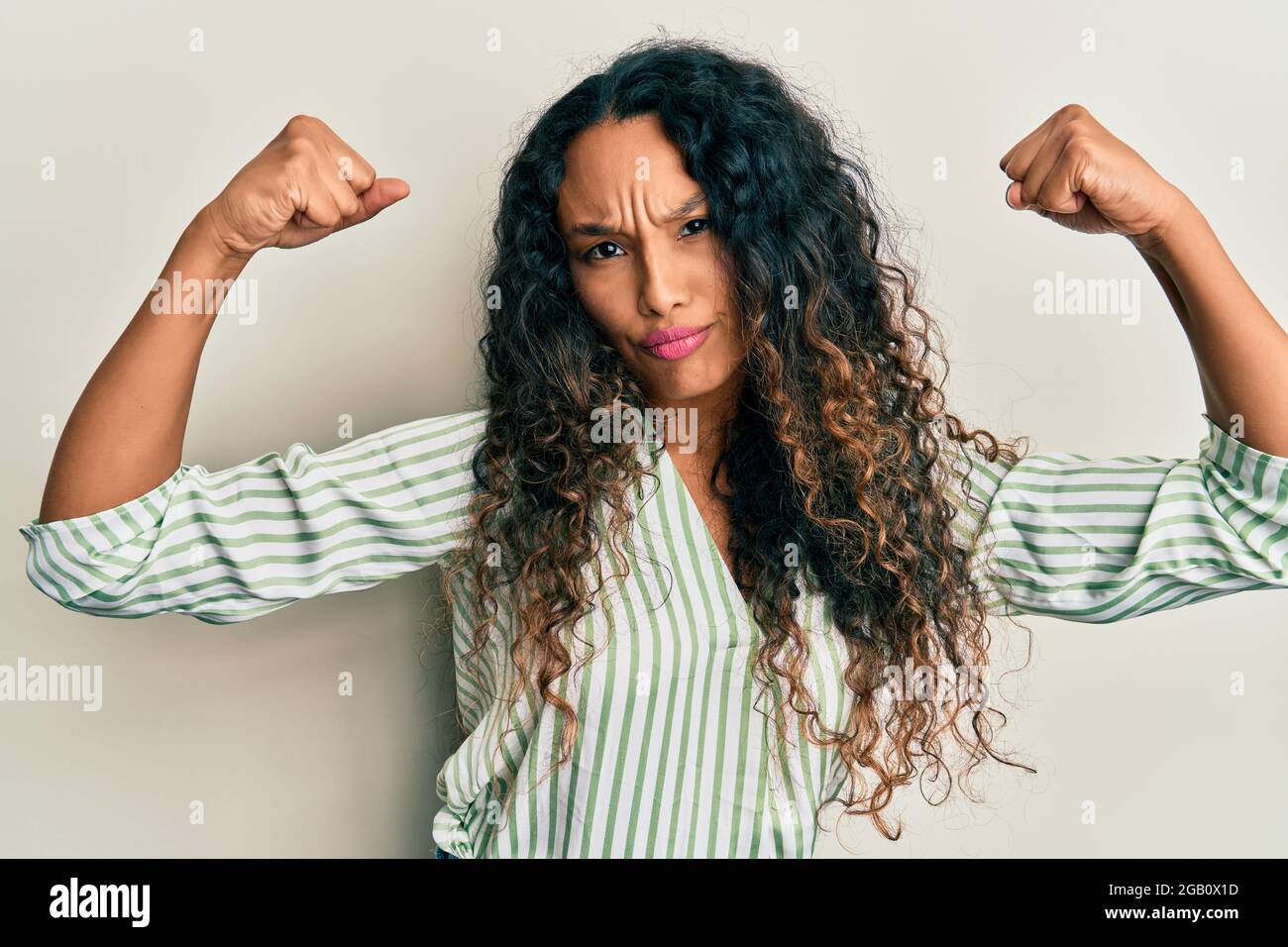 Young latin woman wearing casual clothes showing arms muscles smiling ...