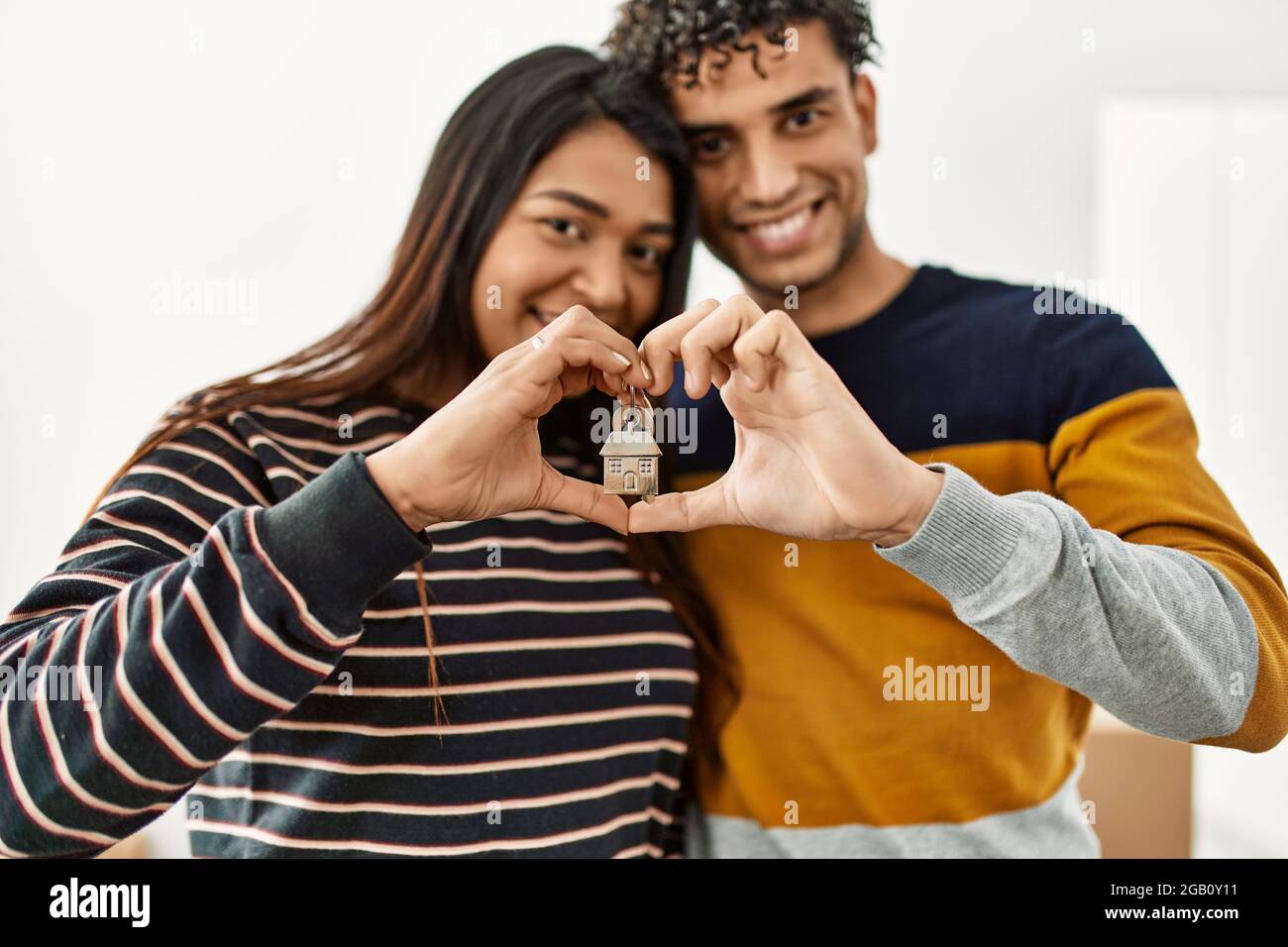 Young latin couple doing heart symbol with hands holding key of new ...