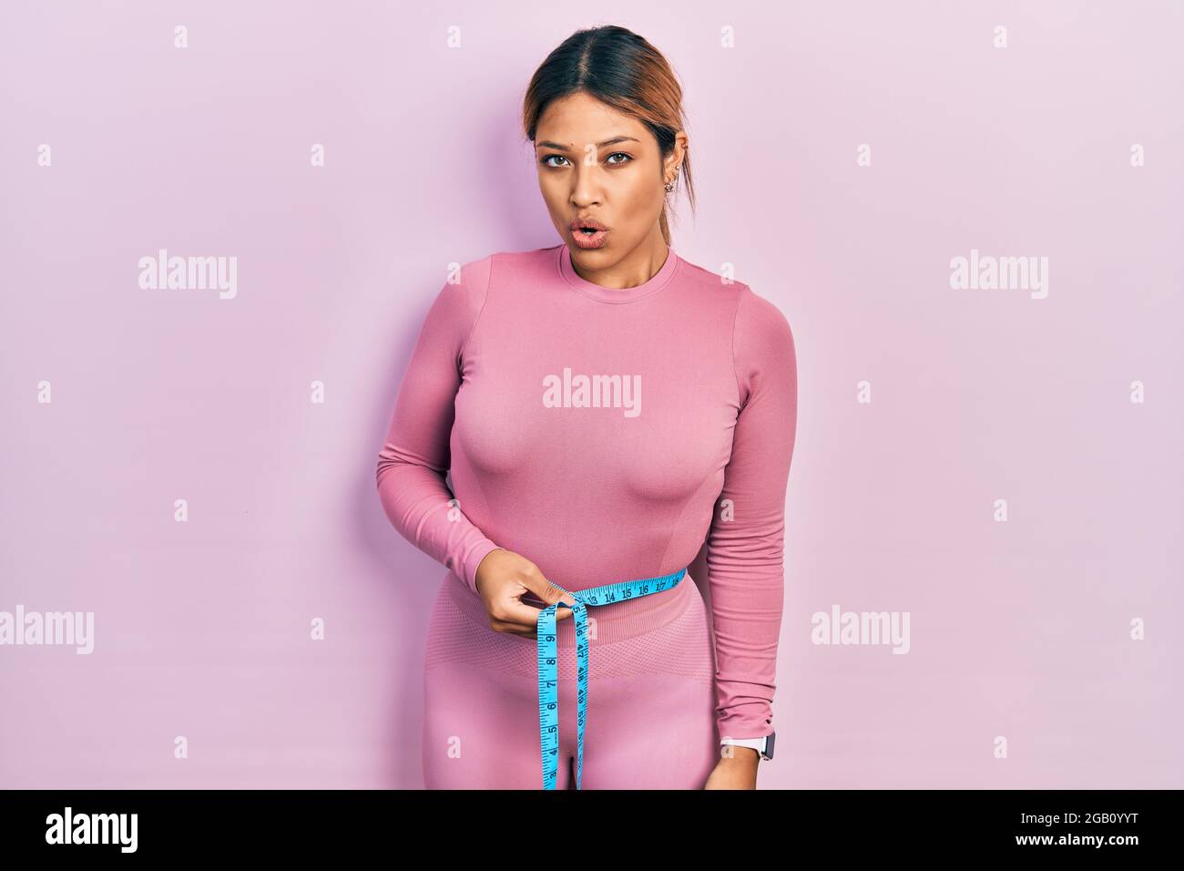 Beautiful hispanic woman using tape measure measuring waist scared and ...