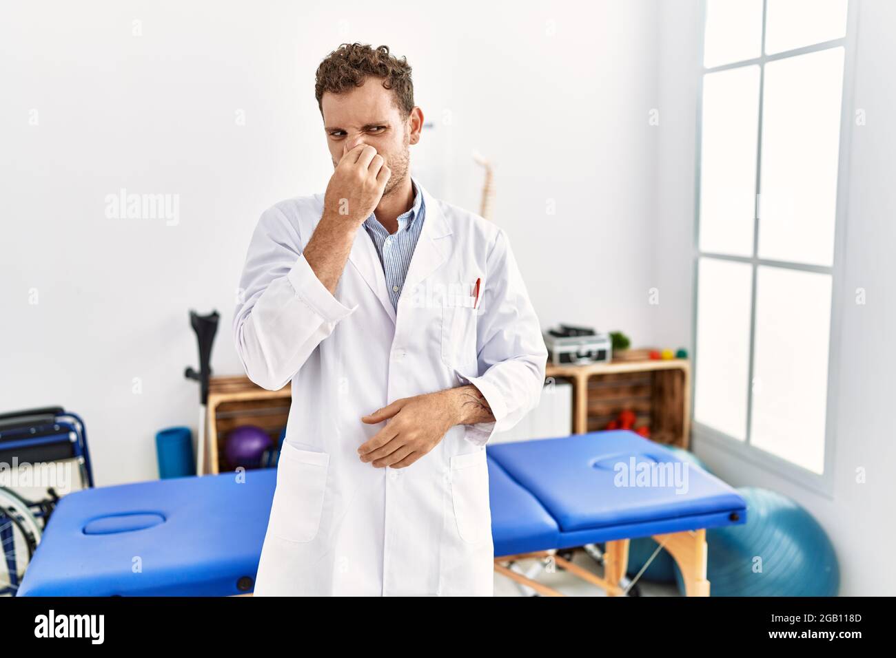 Handsome young man working at pain recovery clinic smelling something ...