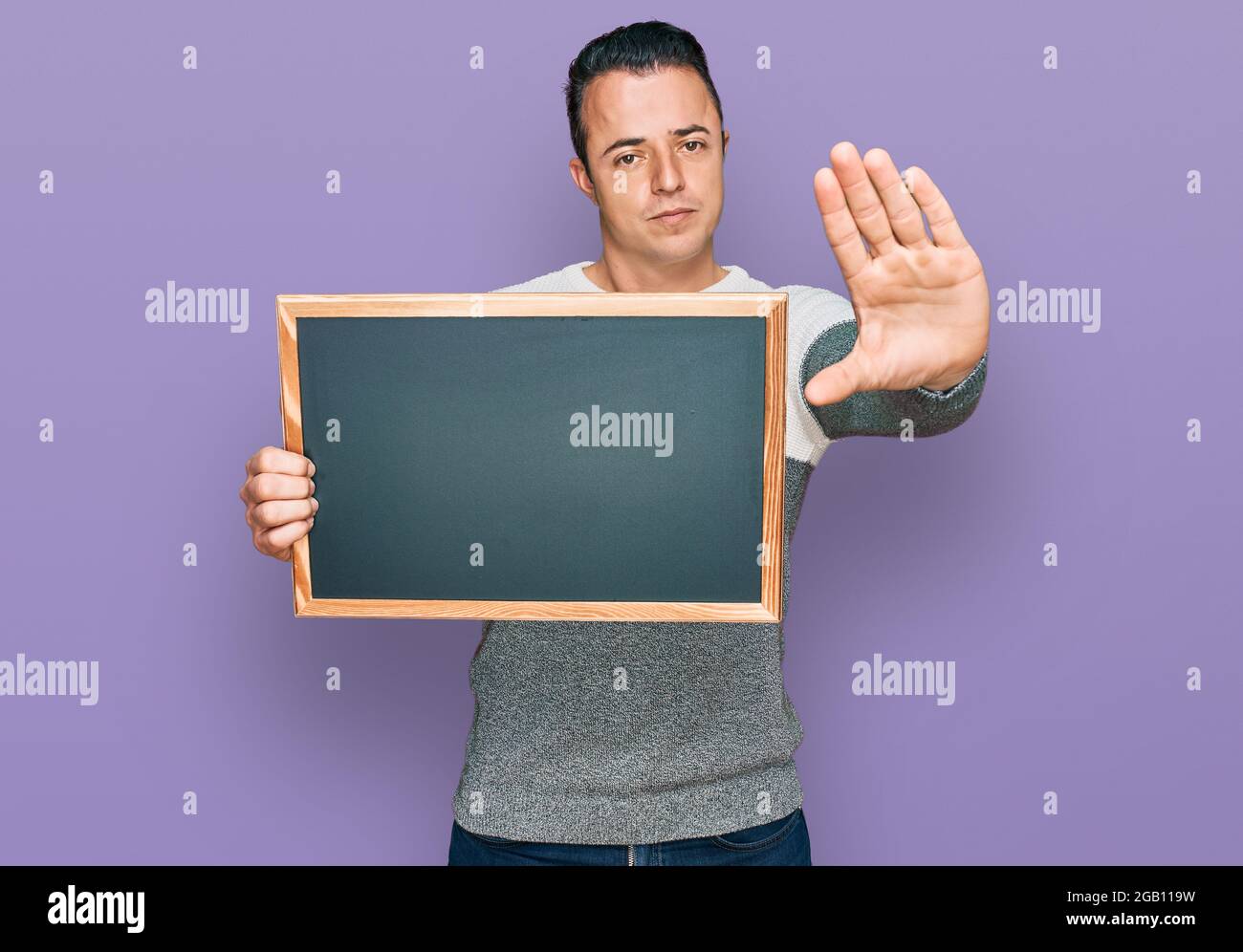 Handsome young man holding blackboard with open hand doing stop sign ...