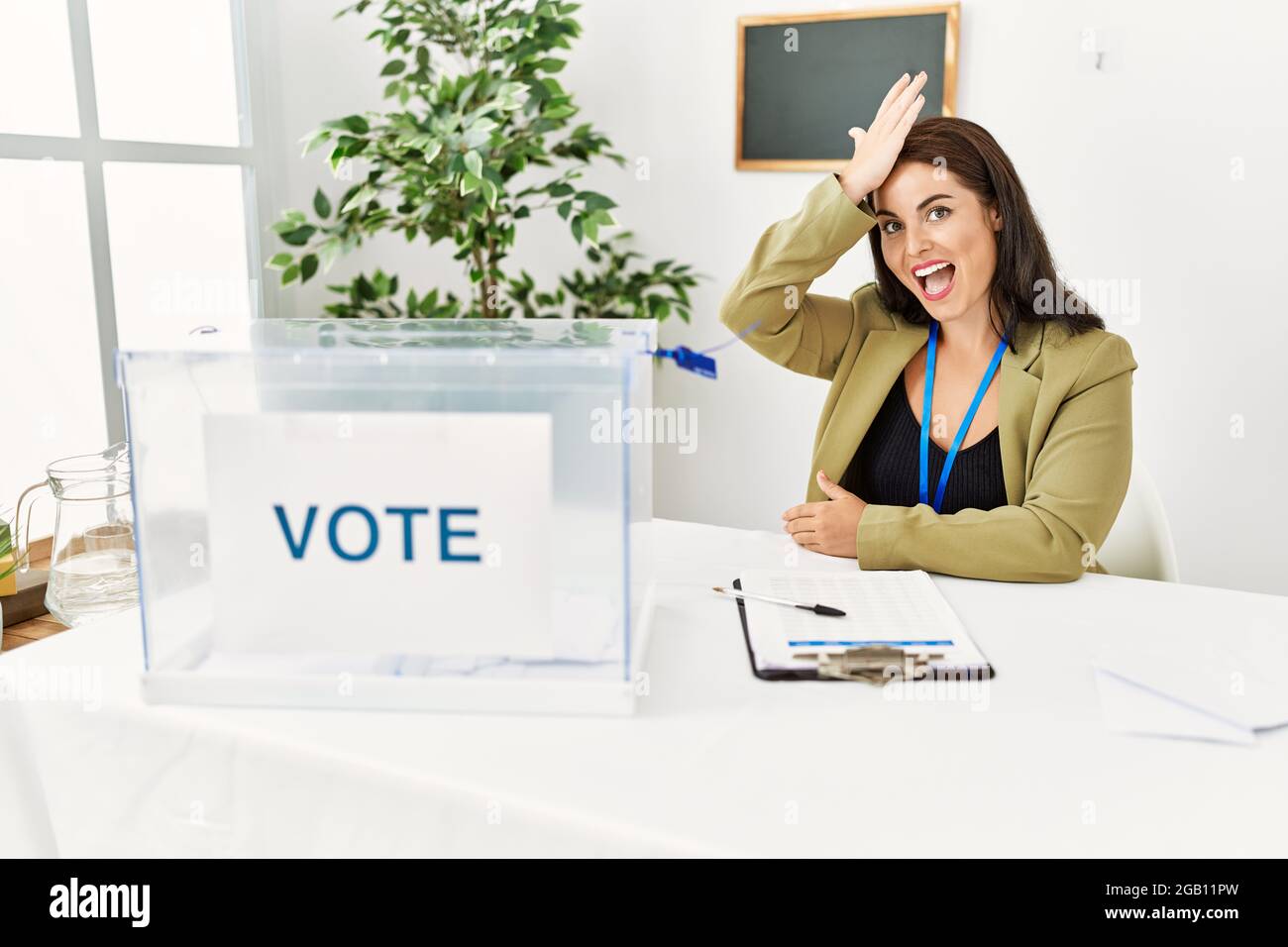 Young brunette woman sitting at election table with voting ballot ...