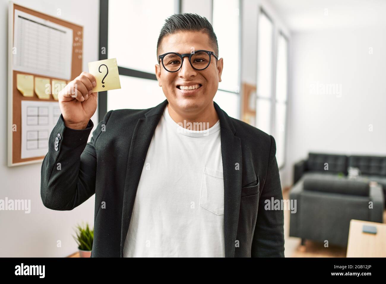 Young latin businessman smiling happy holding question mark reminder at ...
