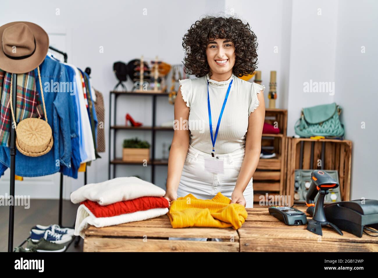 Young middle east shopkeeper woman smiling happy folding sweater at ...