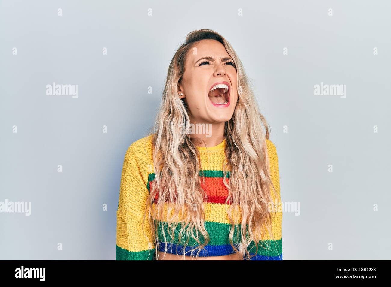 Beautiful young blonde woman wearing colored sweater angry and mad ...