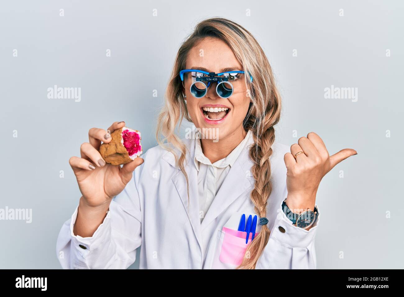 Beautiful young blonde woman holding geode stone wearing magnifier ...