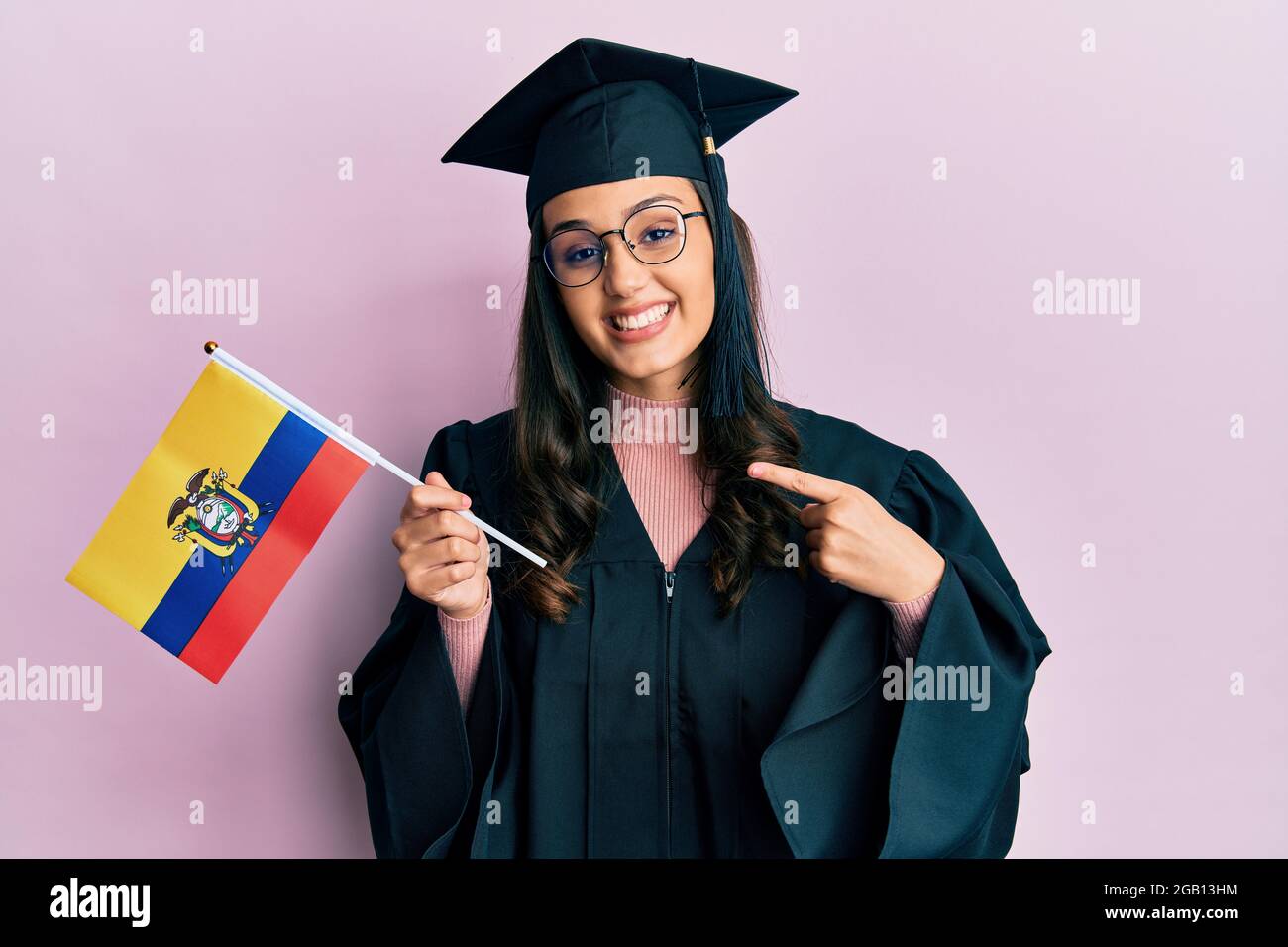Young hispanic woman wearing graduation uniform holding ecuador flag ...