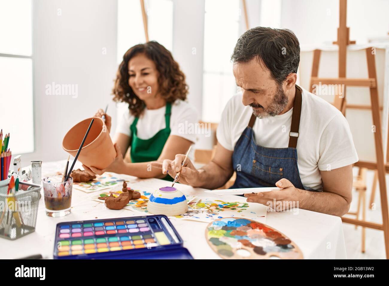 Two middle age students smiling happy painting clay sculpture at art ...