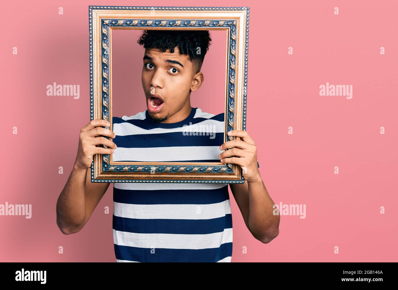 Young african american man holding empty frame in shock face, looking ...