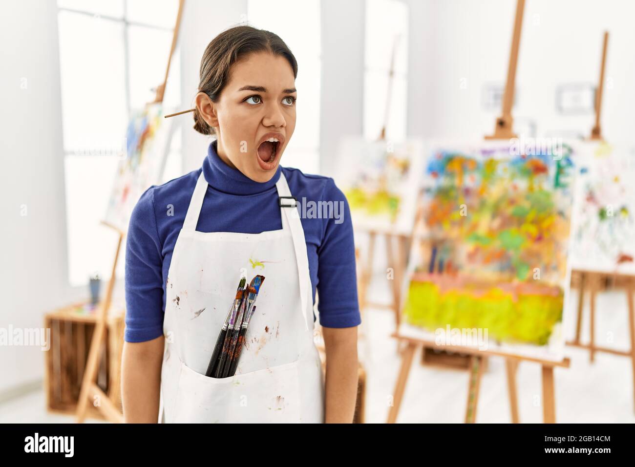 Young brunette woman at art studio angry and mad screaming frustrated ...