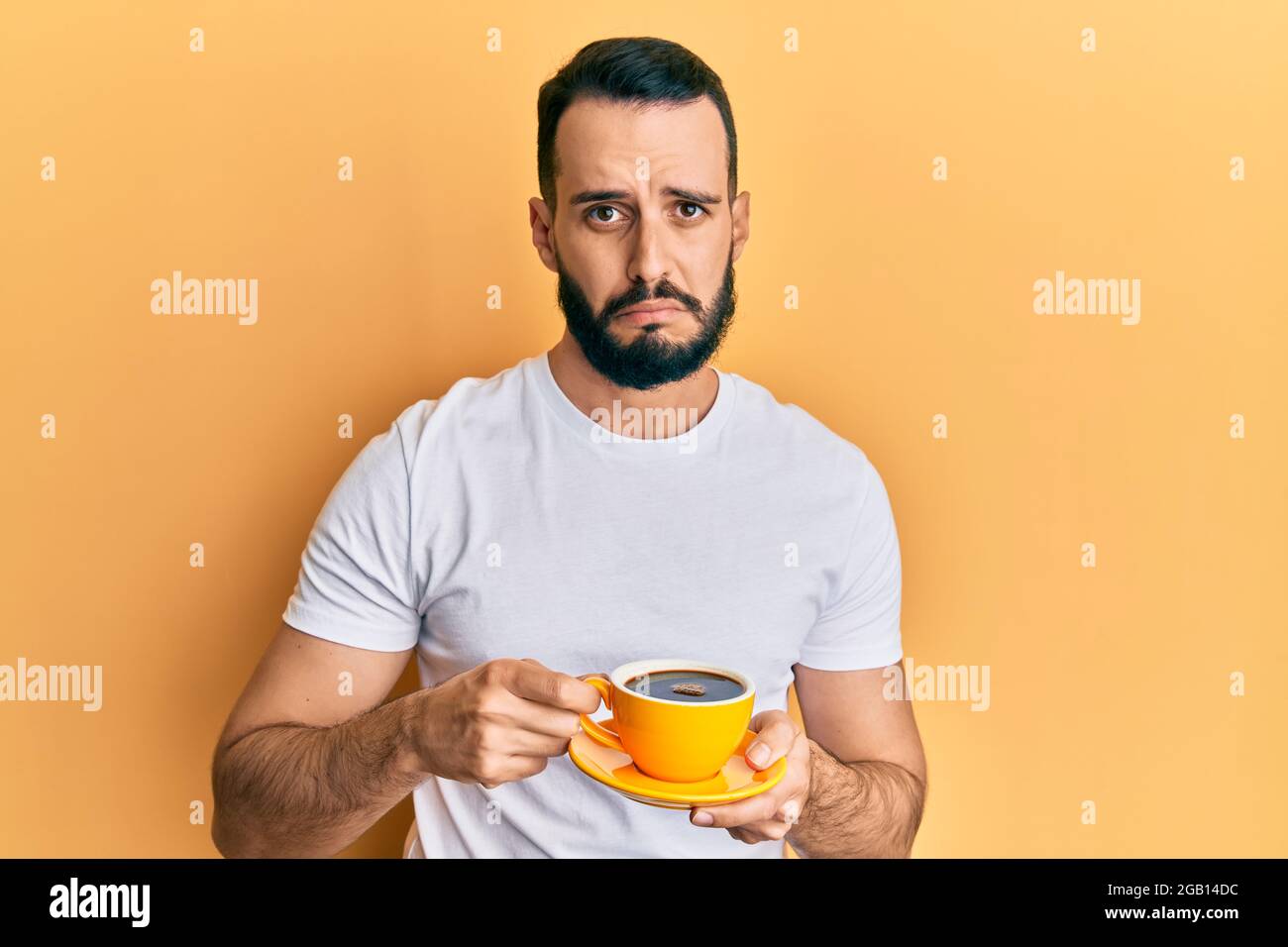 Young man with beard drinking a cup coffee depressed and worry for ...