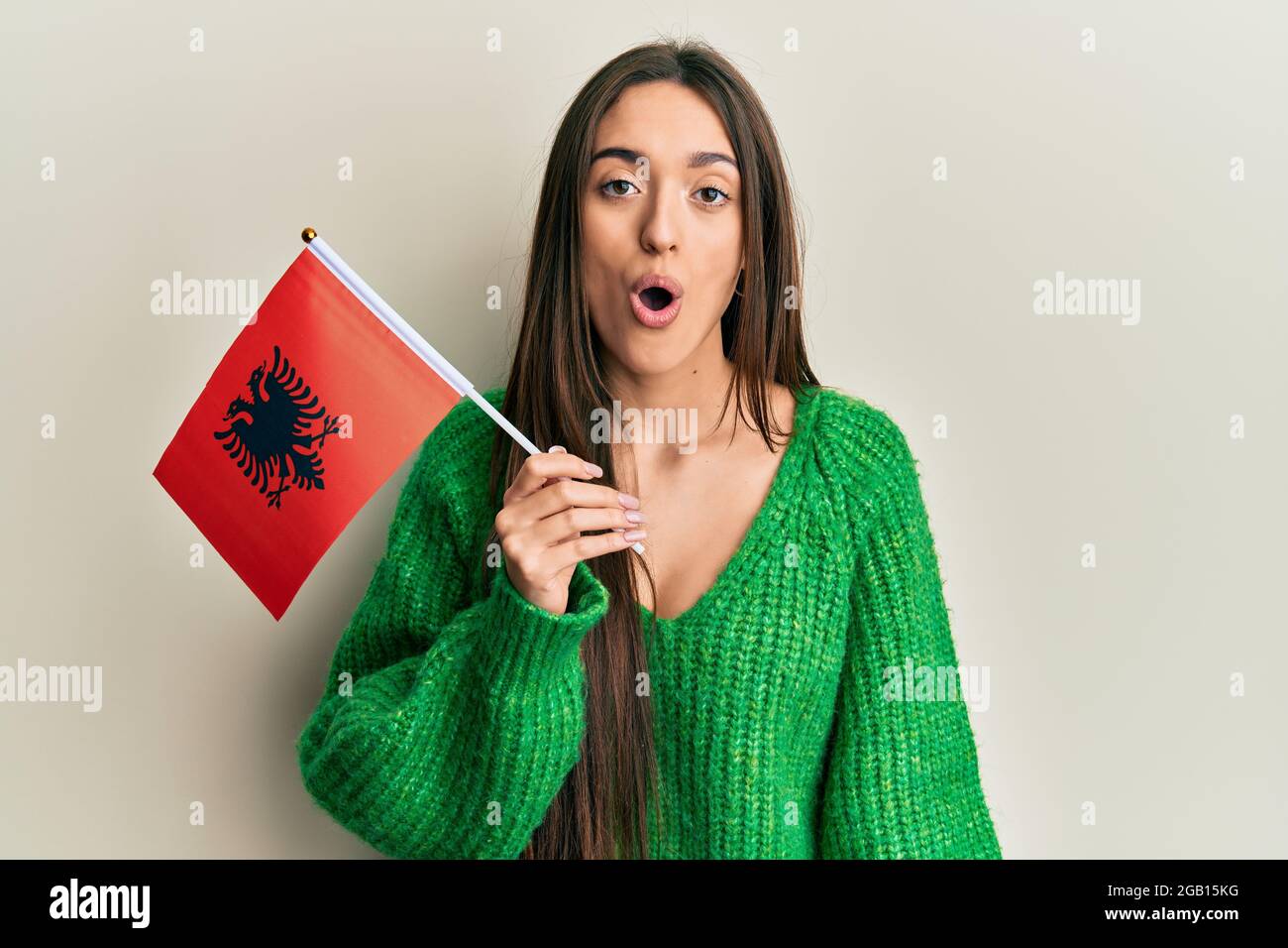 Young hispanic girl holding albania flag scared and amazed with open ...