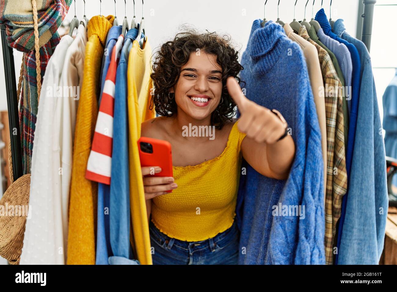 Young hispanic woman searching clothes on clothing rack using ...